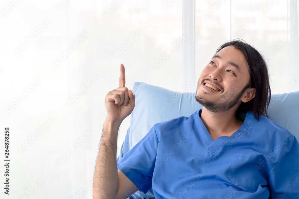 Smiling asian patient sitting on hospital bed with finger pointing up ...