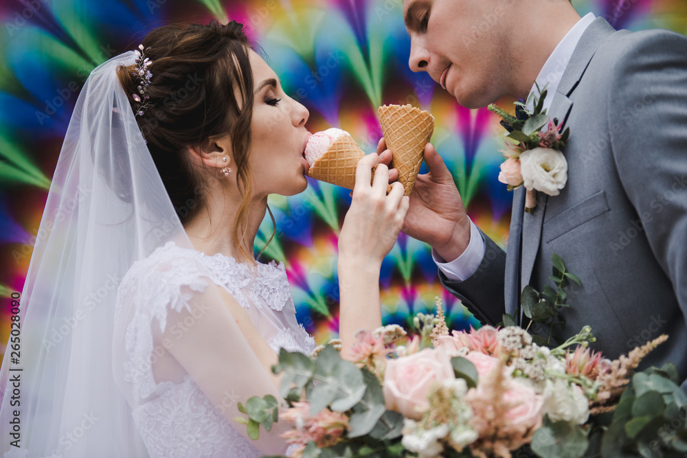 The bride and groom are eating ice cream together on a bright wall ...