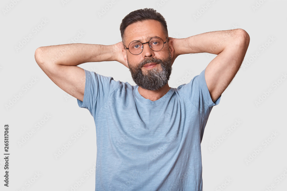 Confident relaxed calm man rises his arms, touching his head with both ...