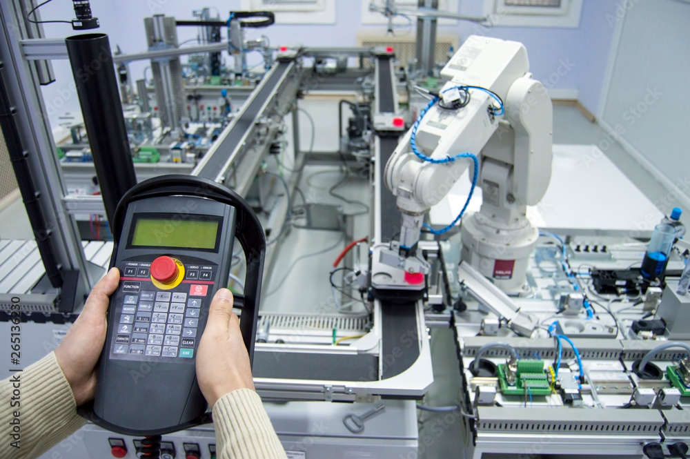 Man is holding teach panel (tablet) to control a robot arm which is ...