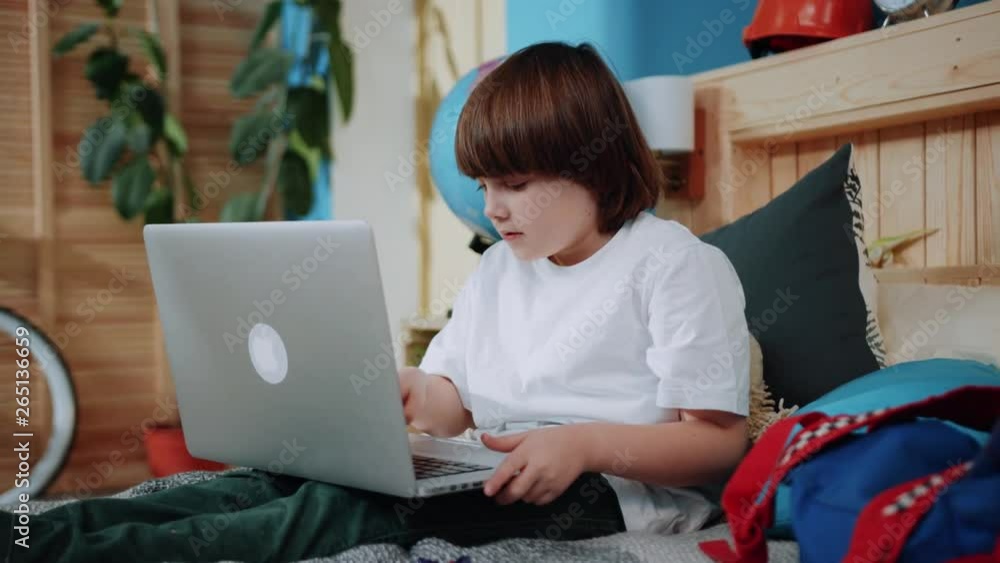 Vidéo Stock Serious little boy with laptop lying on the bad at home ...
