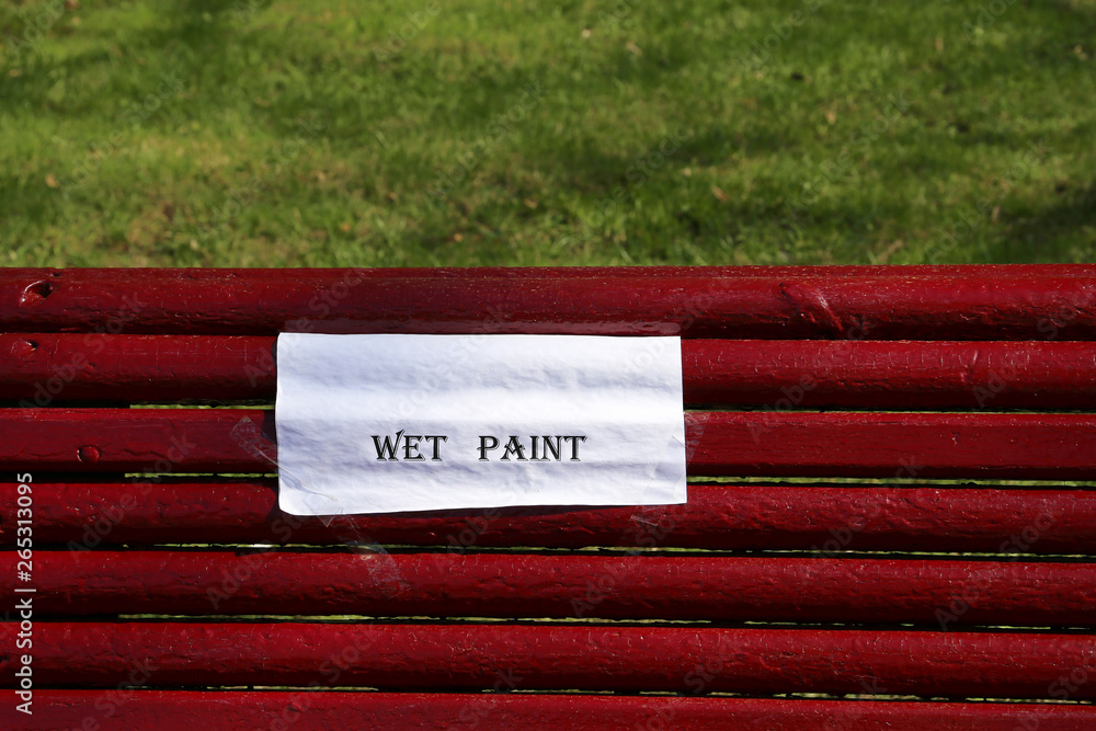Inscription 'Wet paint' on a sheet of white paper on red wooden bench ...