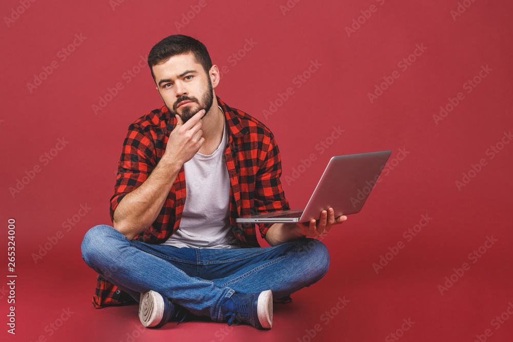 A young sad man sitting on the floor with a crossed legs putting his ...
