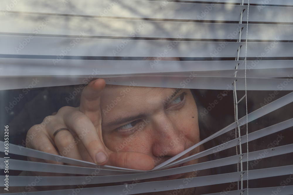 Man watching through window blinds Portrait of young thoughtful male ...