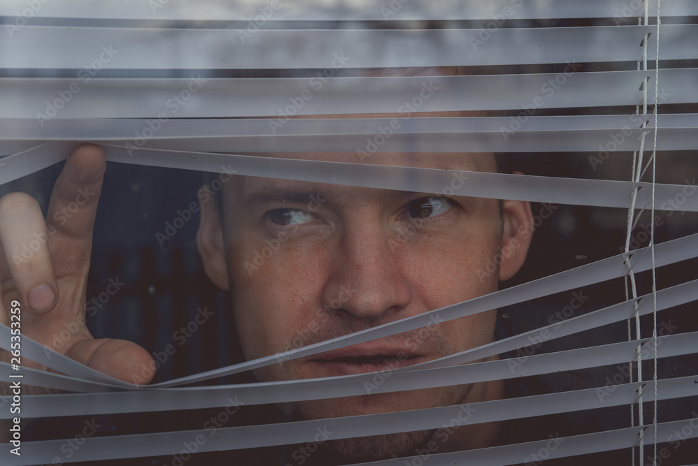 Man watching through window blinds Portrait of young thoughtful male ...