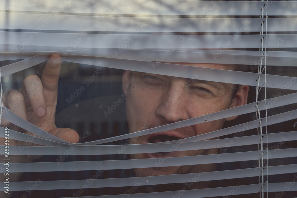 Man watching through window blinds Portrait of young thoughtful male ...