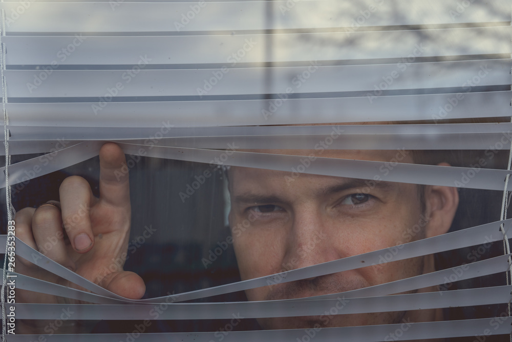 Man watching through window blinds Portrait of young thoughtful male ...