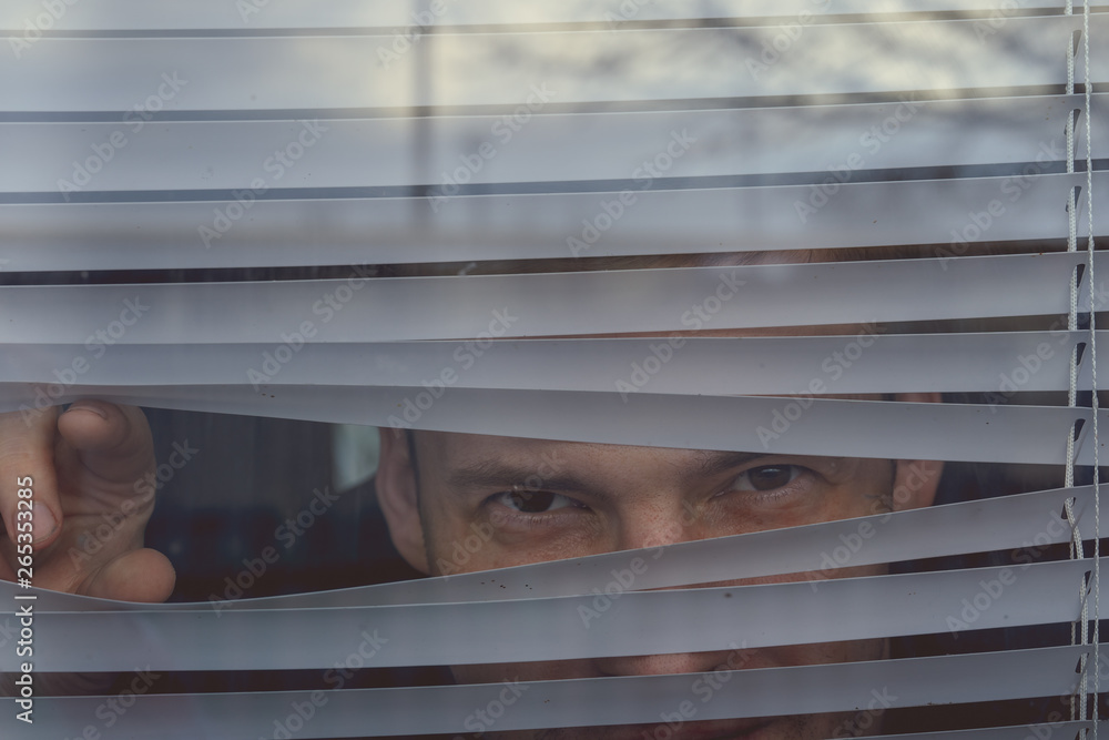 Man watching through window blinds Portrait of young thoughtful male ...