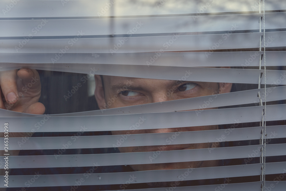 Man watching through window blinds Portrait of young thoughtful male ...