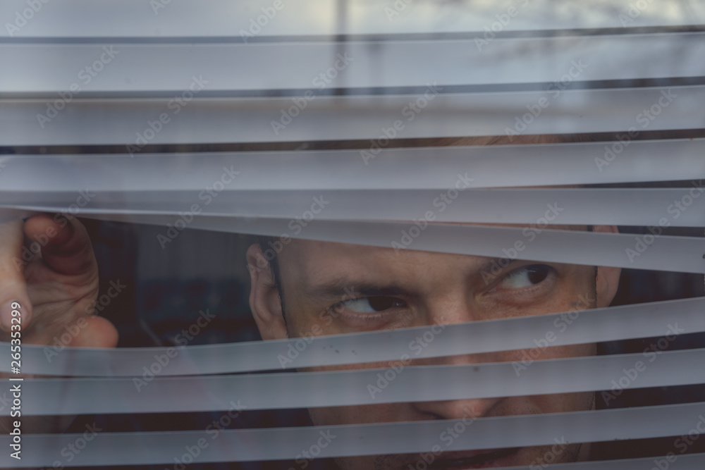 Man watching through window blinds Portrait of young thoughtful male ...