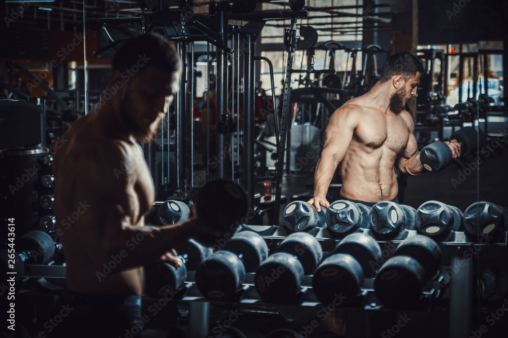 Good looking young man bodybuilder lifting dumbbells and working on his ...