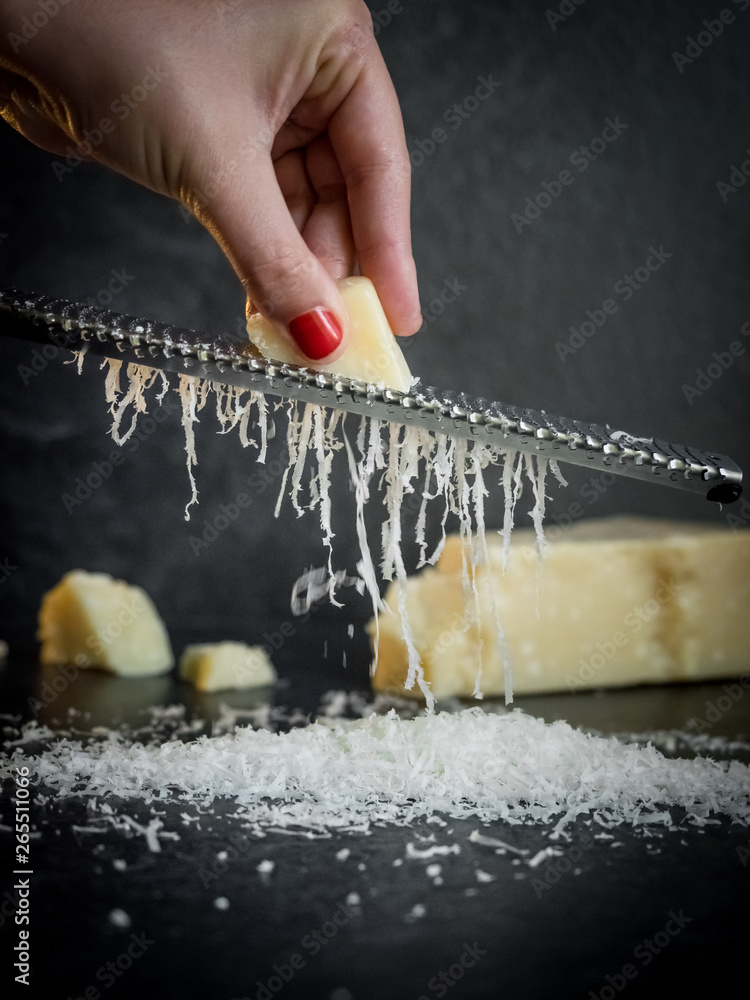 Hand of a woman grating parmesan cheese on a black background. Dark ...