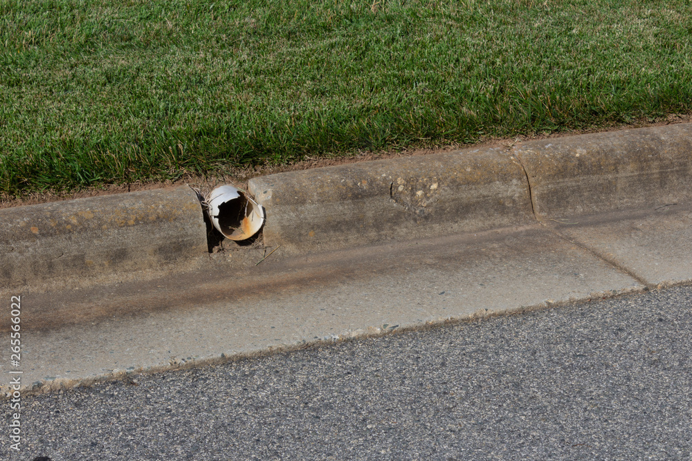 White PVC pipe emerging from formed concrete curb, green grass and ...