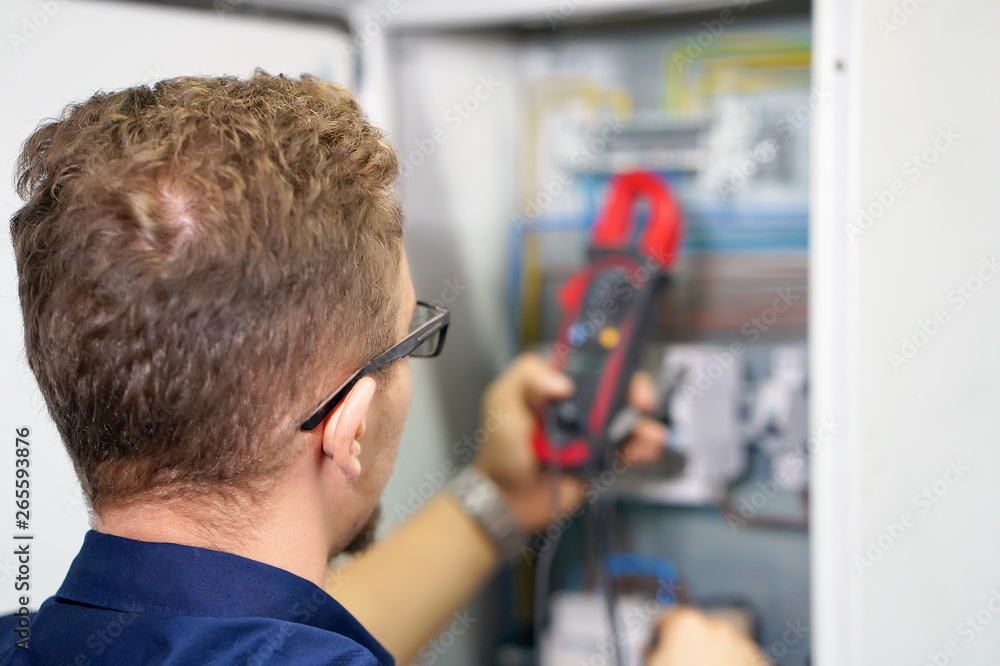 Electrician measures voltage with multimeter in electrical cabinet. An ...