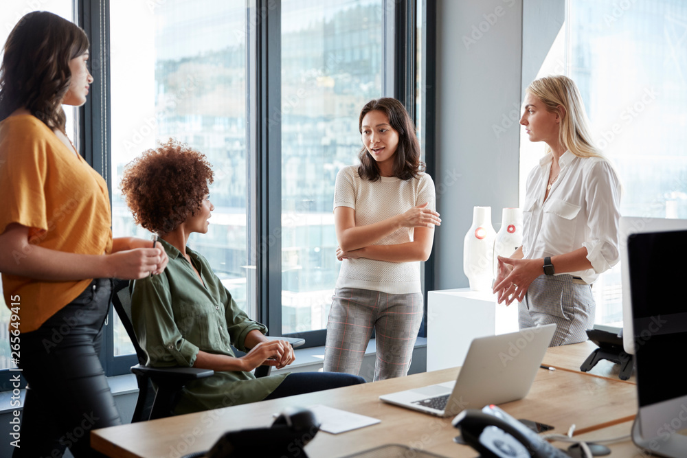 Four female colleagues in discussion at a desk in a creative office ...