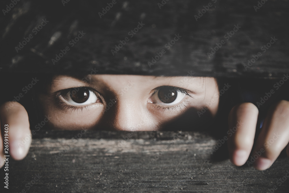 Bored little girl, Frightened child is spying through a wooden fence ...