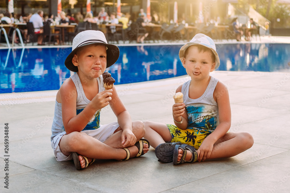 two pre-school boys in hats sit by the hotel's outdoor pool and eat ice ...