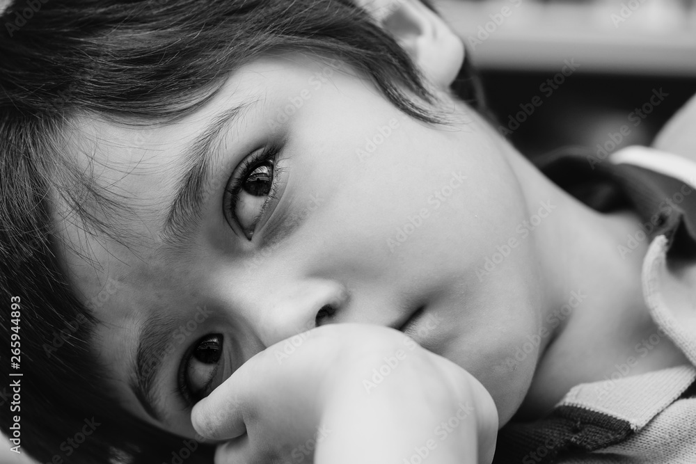 Emotional portrait of sad boy sitting alone on table and looking up with thinking face, Cropped ...