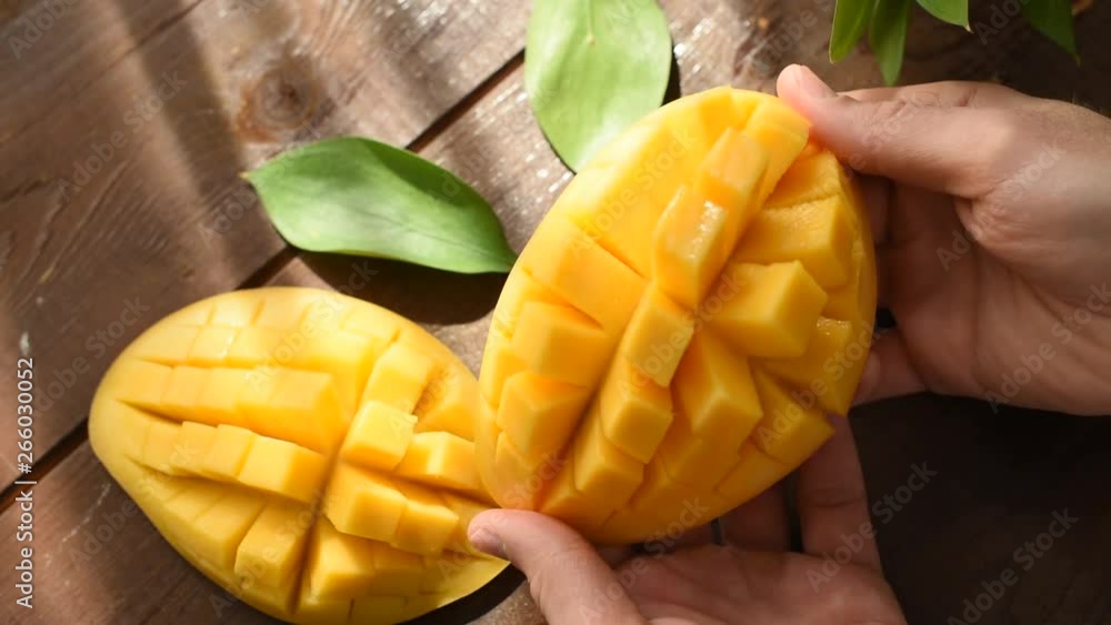 Person opens cut mango over wooden table background, closeup view ...