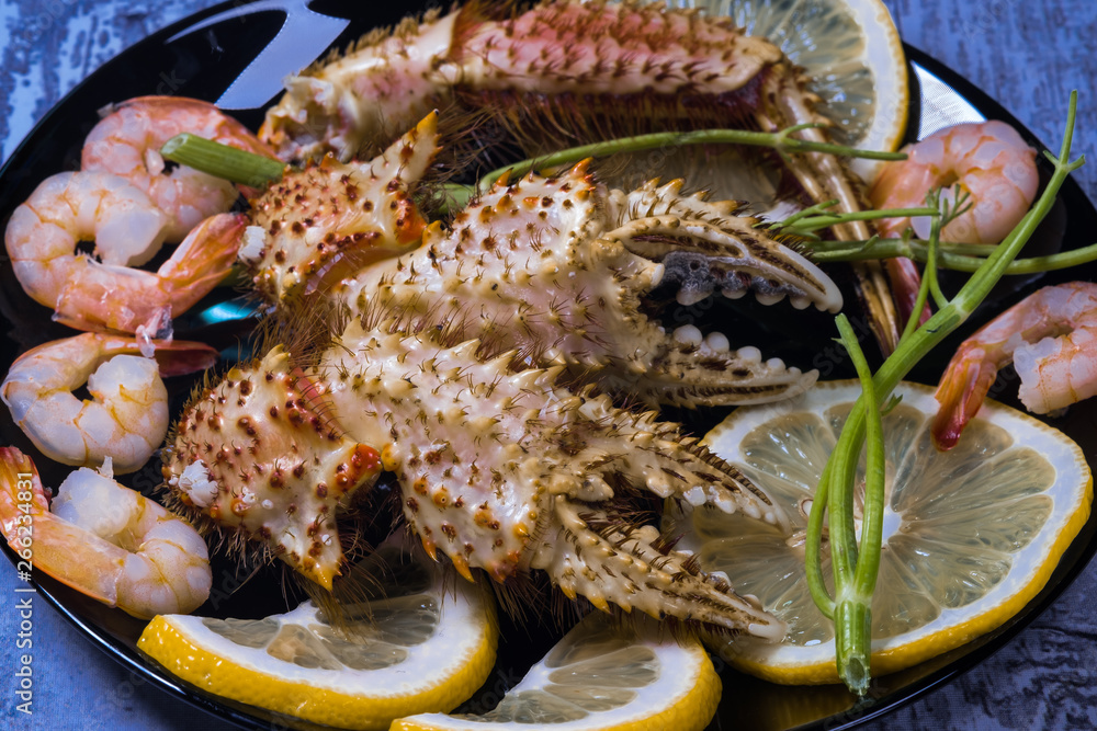 Seafood. Tentacles and claw of a crab with shrimp on a black plate ...