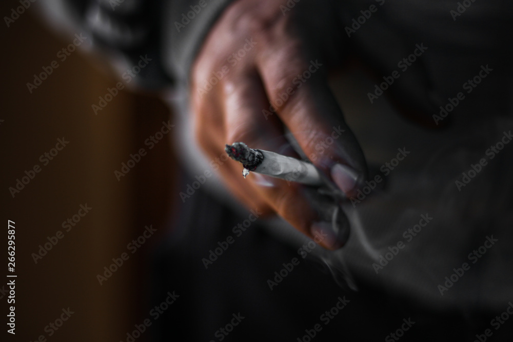 closeup a man's hand holding a crumpled, smoldering cigarette with ...