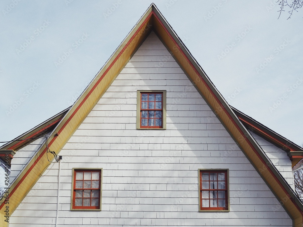 peak of a pointy old house with white siding and three windows that ...