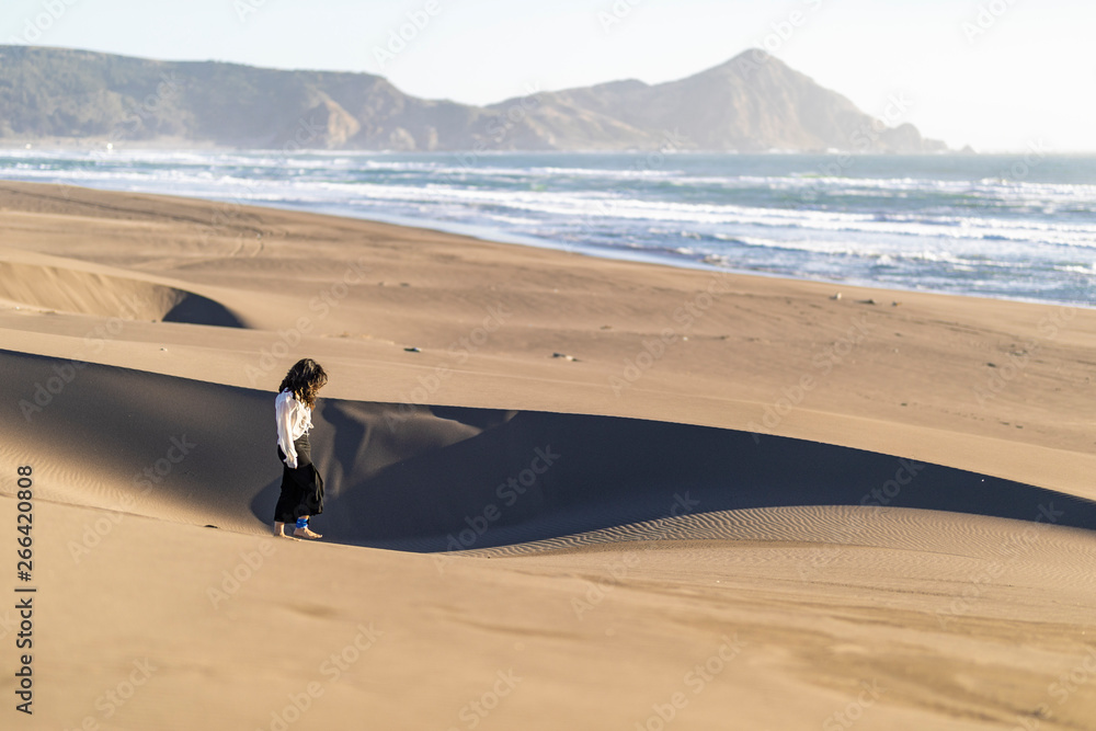Beautiful young girl walking along the beach sand dunes step by step ...