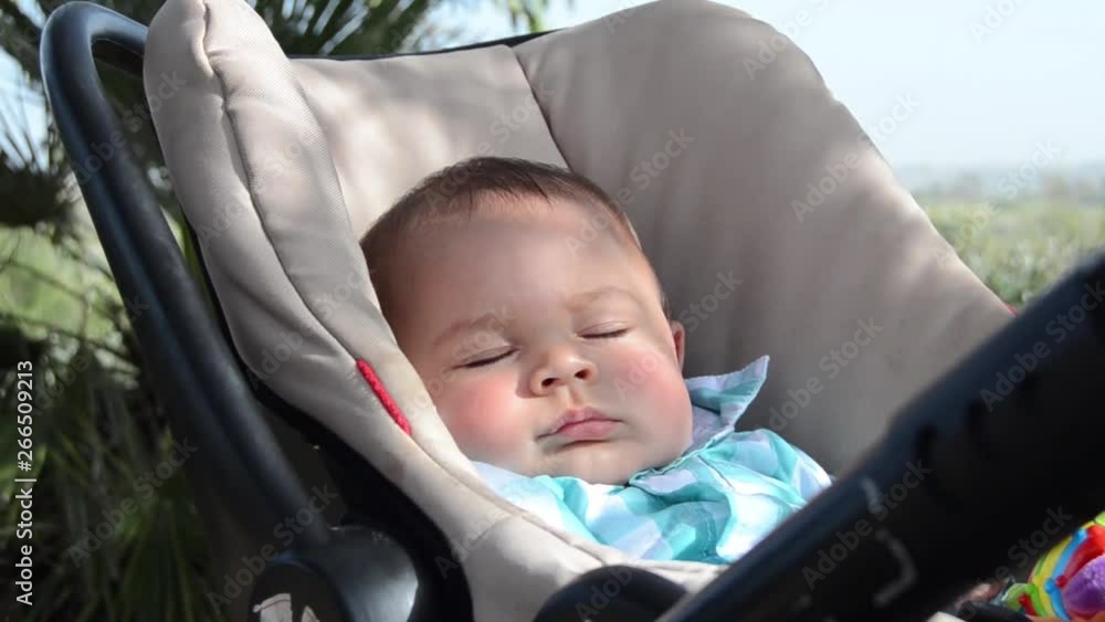 Cute six months old baby boy sleeping in the pushchair in the shadow of ...