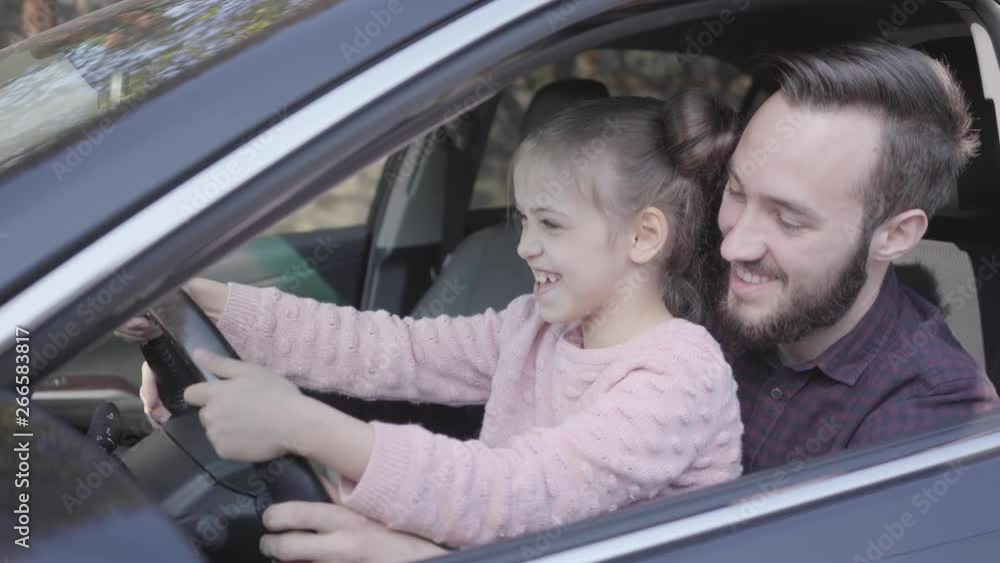 Little girl sitting on father's lap in the car close up. The child is ...