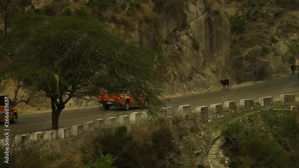 Seveal orange vehicles drive along a mountain road between a stone wall ...