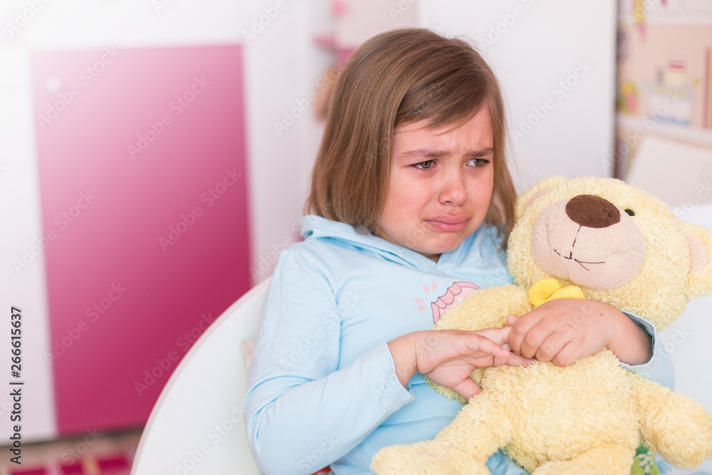 Cute adorable little girl crying in children's room hugging teddy bear ...