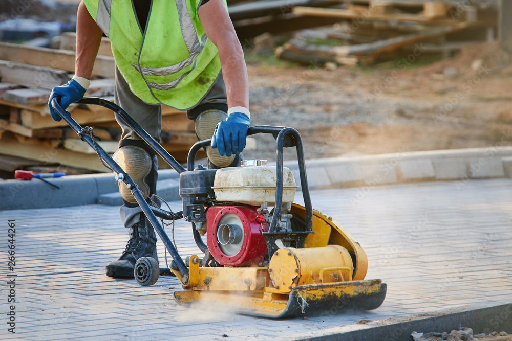 Foto de Worker in uniform and knee pads use vibratory plate compactor ...