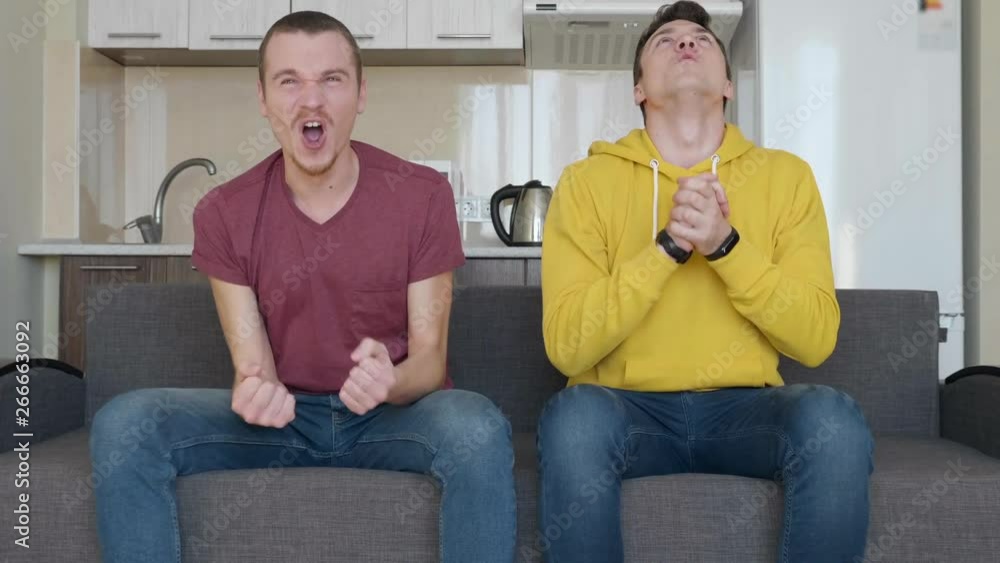 Two men sitting on the couch watch a football match on TV and enjoy the ...