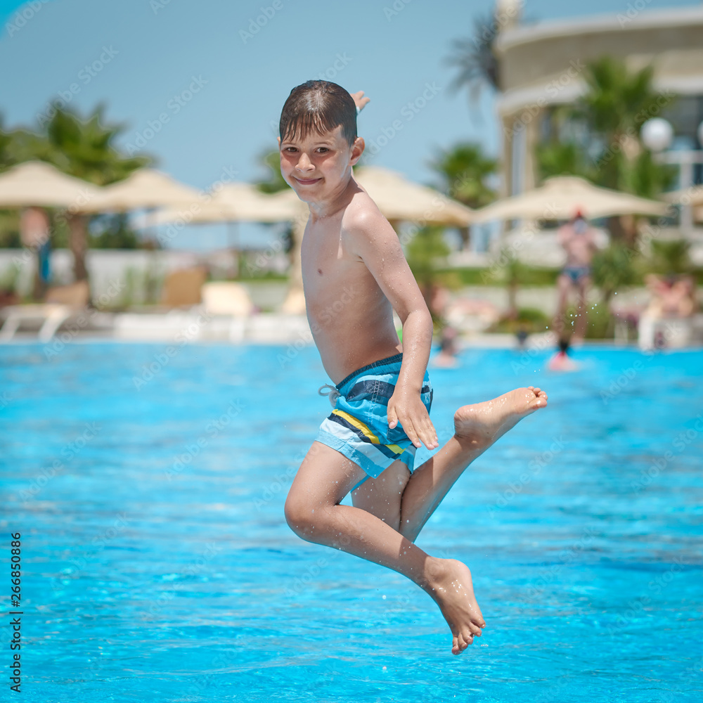 Caucasian boy spending time in pool at resort. He is making high jump ...