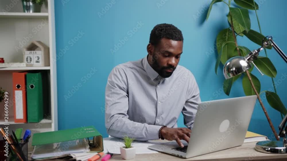 Cheerful positive young afro American man actively working with laptop ...