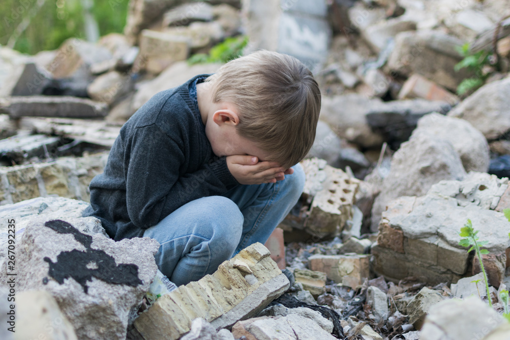 Little boy near the destroyed house. Child trouble, loneliness concept ...