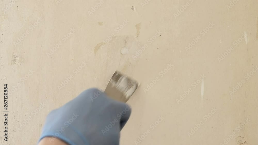 Hand of repairman in blue glove with putty knife is applying paste on a ...
