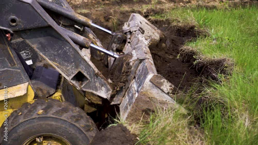 partial view of mini loader removing layer of grassy soil during earth ...