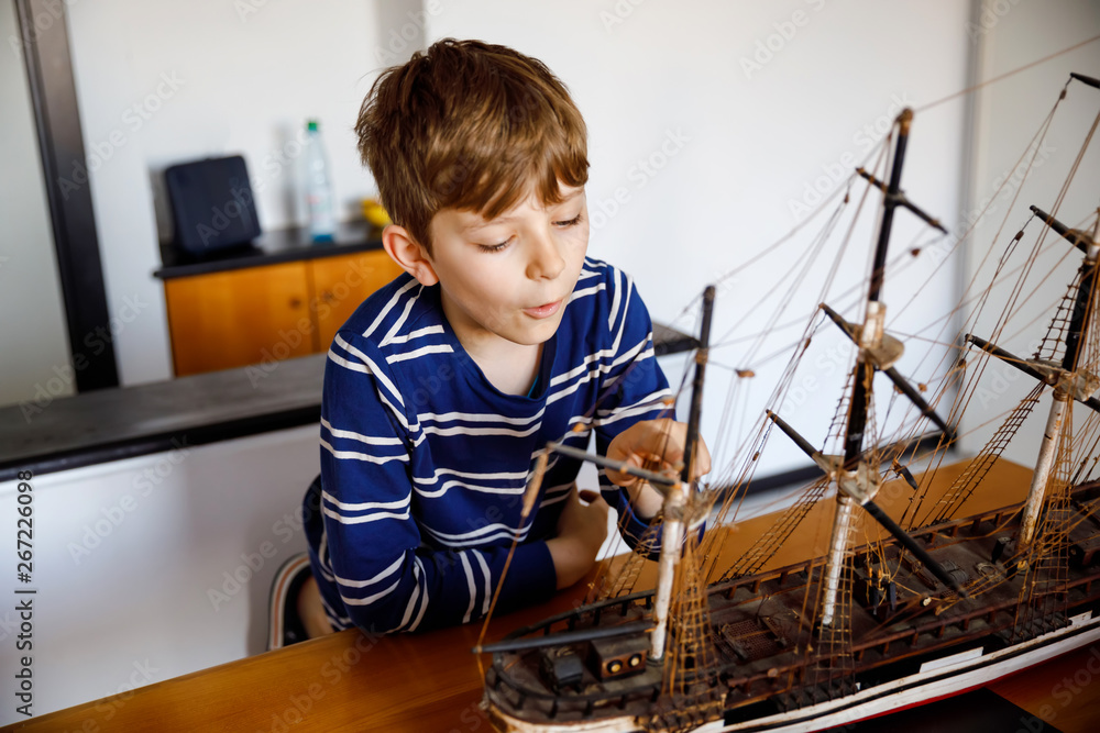 Little blond school kid boy playing with sailing ship model indoors ...