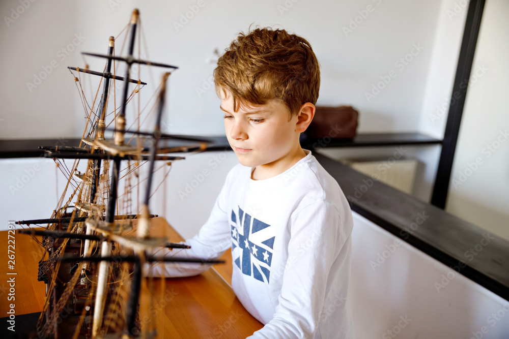 Little blond school kid boy playing with sailing ship model indoors ...