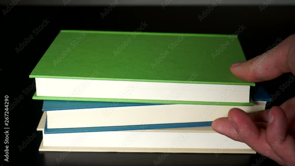 Hand grabs books from a stack then puts them back. A hand grabbing ...