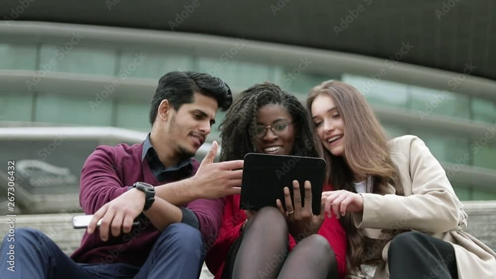 Bottom view of three young people sitting outside, googling on tablet ...