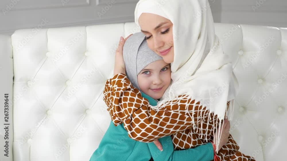 Muslim family mom and her little daughter in hijabs are hugging sitting ...