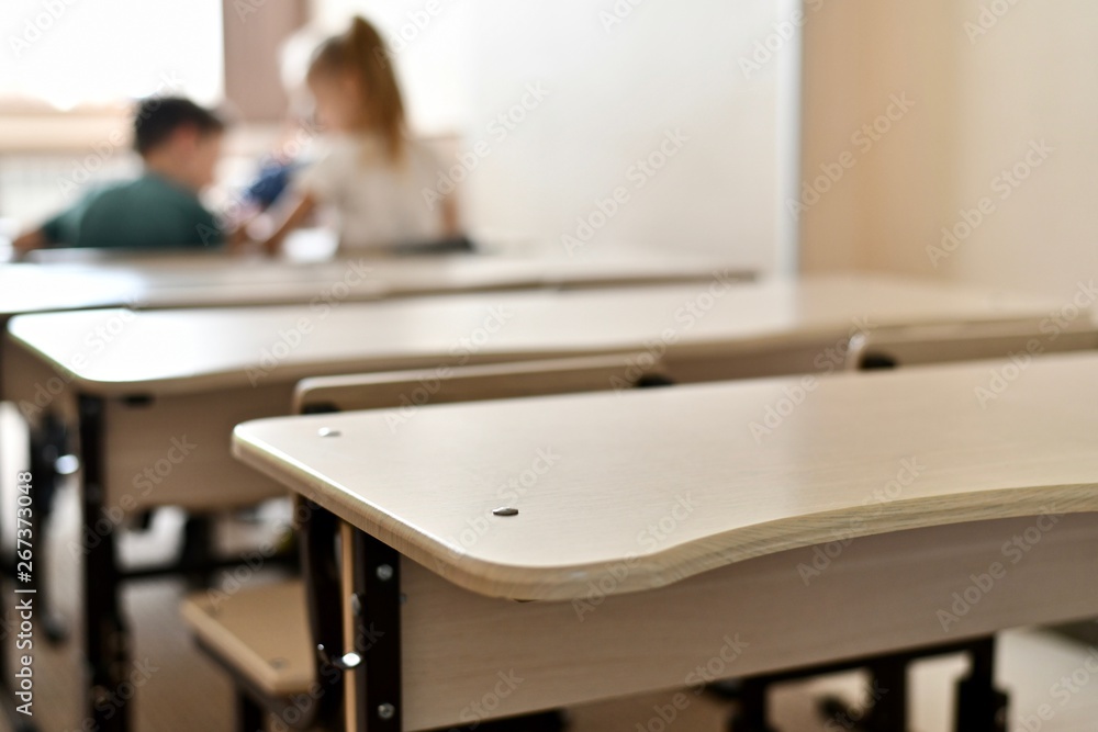 A row of school desks, the last empty tabletop in focus. At the first ...