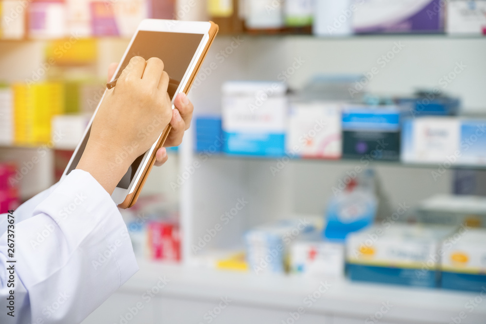 Pharmacist working with a tablet computer in the pharmacy holding it in ...