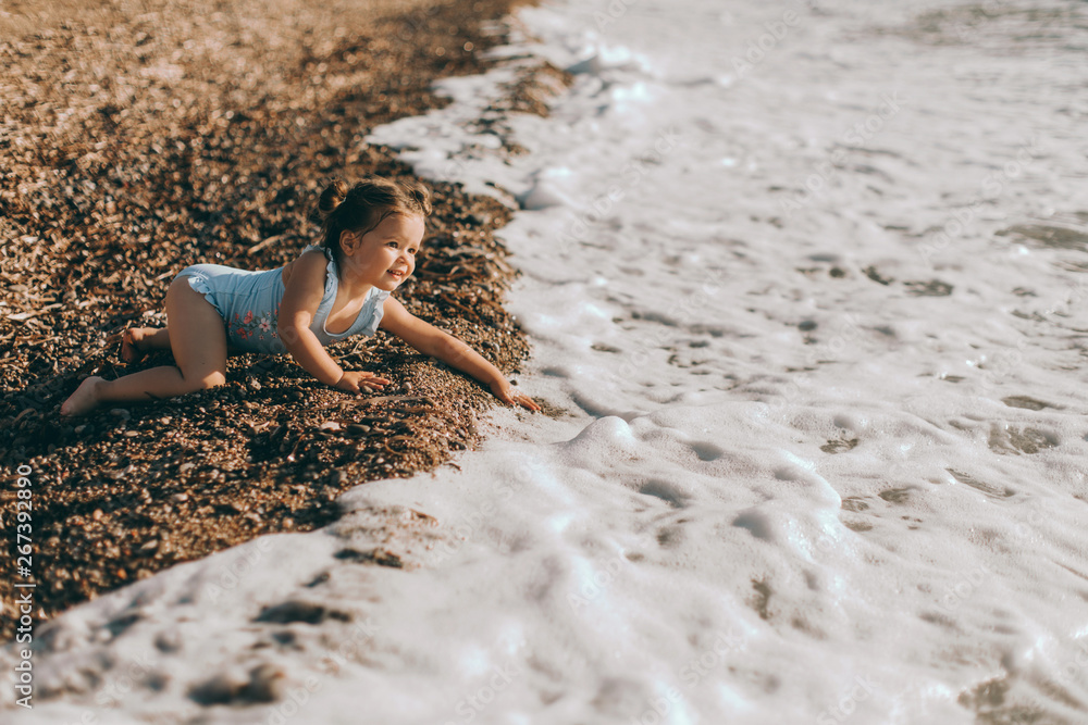 A cute little girl in blue swimsuit playing with a wave on the beach on ...