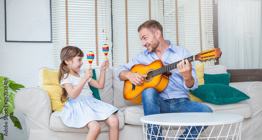Portrait of family man little girl playing guitar and maracas in living ...