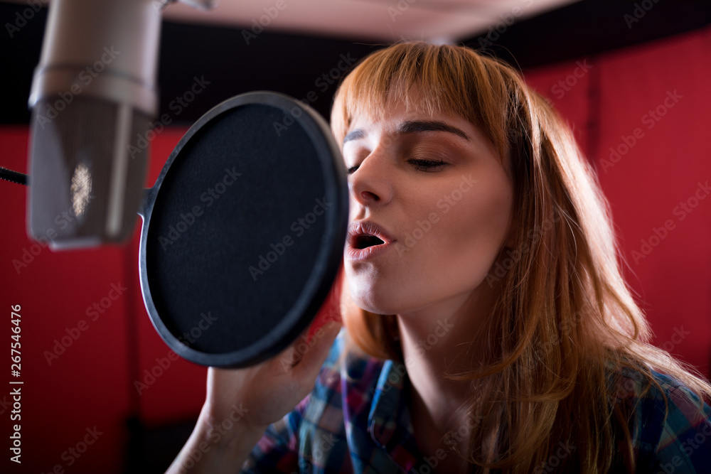 Female with microphone recording a voice for dubbing in music studio ...