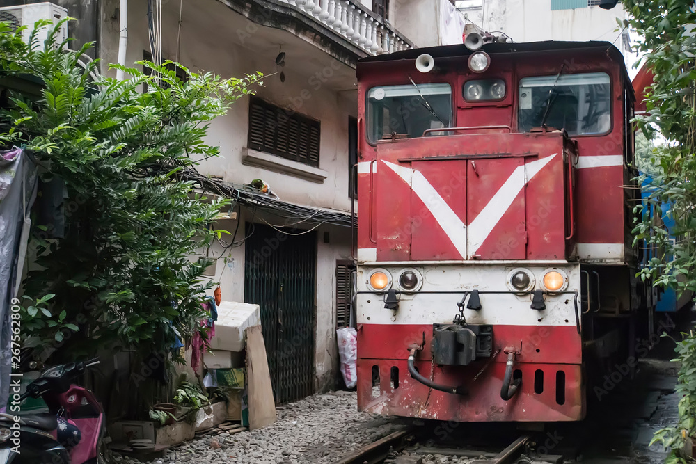 red train locomotive travels though a narrow street in a poor ...