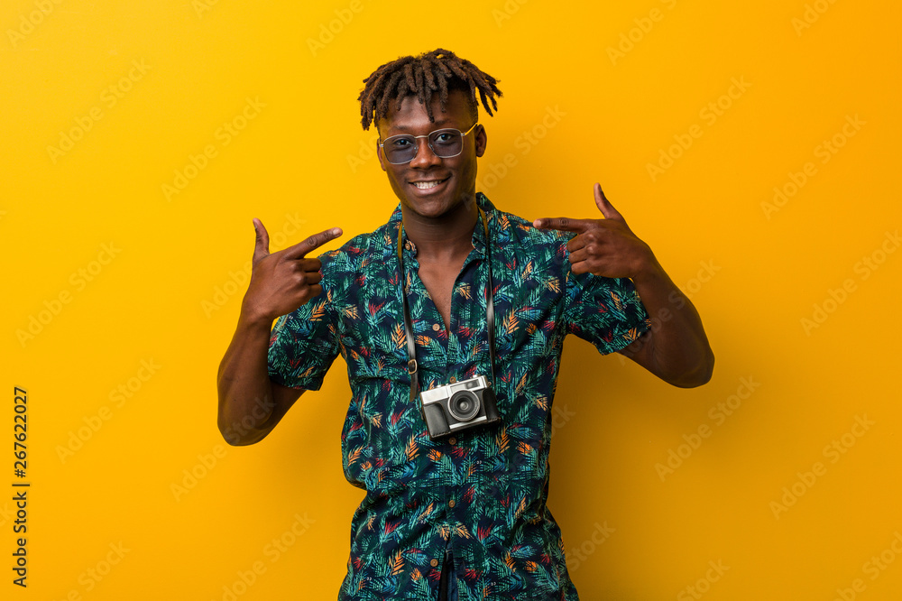 Young black rasta man wearing a vacation look smiles, pointing fingers ...